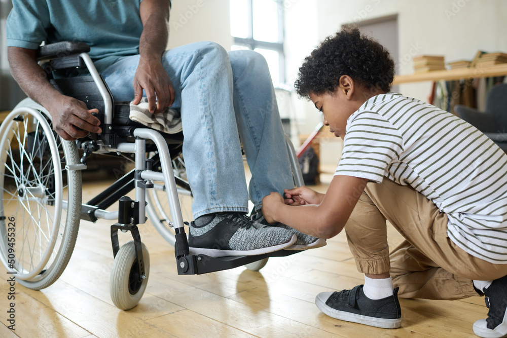 Foto de African little boy helping his disabled father in wheelchair to ...