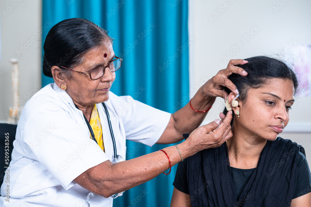 Doctor fixing or inserting hearing air machine or device to impaired ...