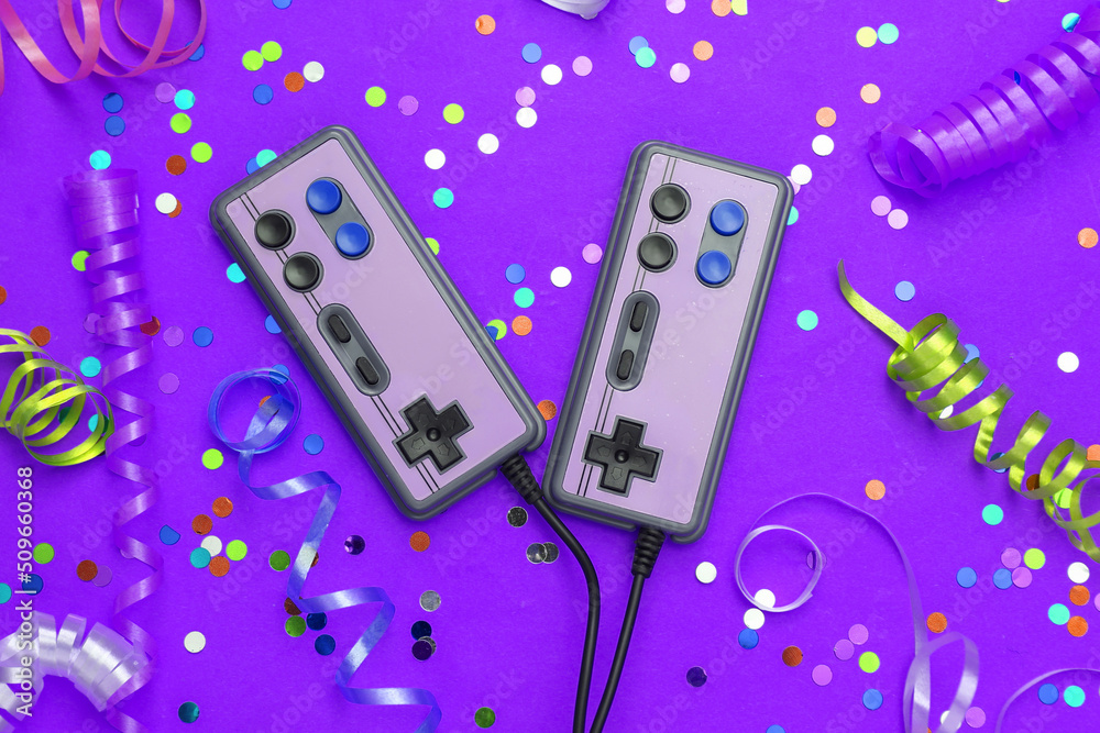 Retro gamepads and colored streamer with confetti on purple background ...