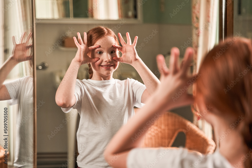 Reflection of the cute funny child making funny faces and showing it to ...