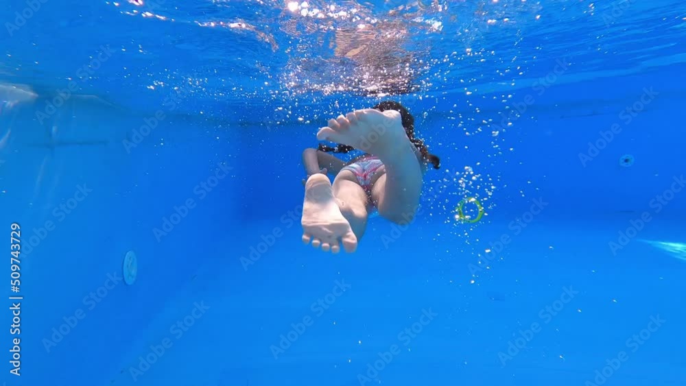Little girl in blue bikini deftly swim underwater in pool by back side ... Little girl in blue bikini deftly swim underwater in pool by back side ...
