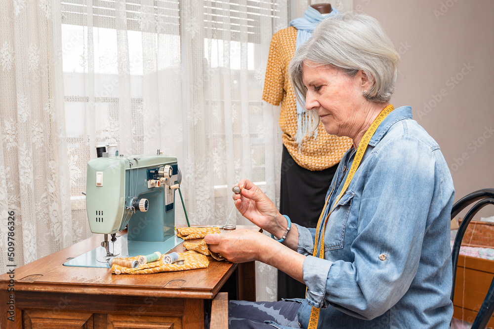 older woman in front of a sewing machine by hand sewing a scrap of ...