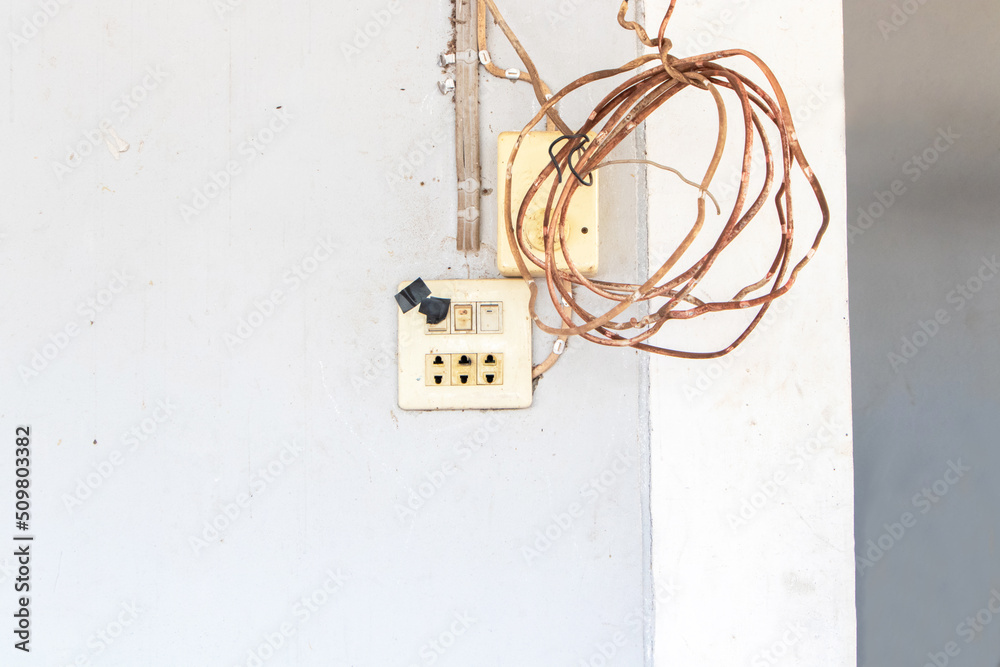 Broken unsafe electric power socket damaged on white wall cordage roll ...