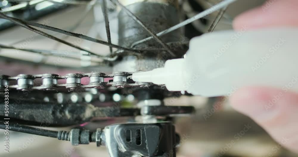 Close-up, lubricating the links of a bicycle chain with bottled oil. A ...