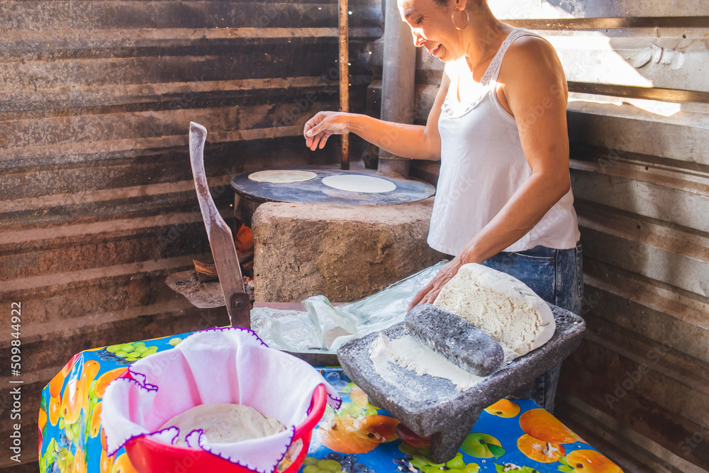 Mujer mexicana torteando maza de maíz en un metate y una estufa de leña ...