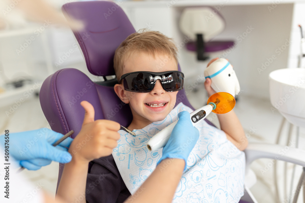 Dental clinic visit. Young positive boy patient showing thumbs up sign ...