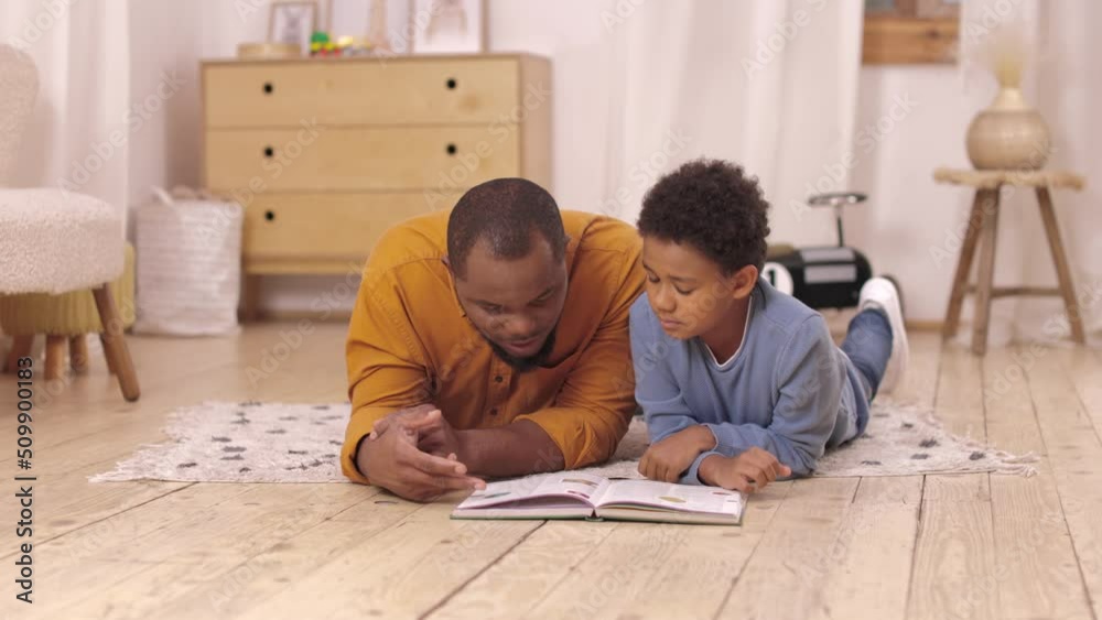 Loving african american dad with schoolboy son lying on floor and ...