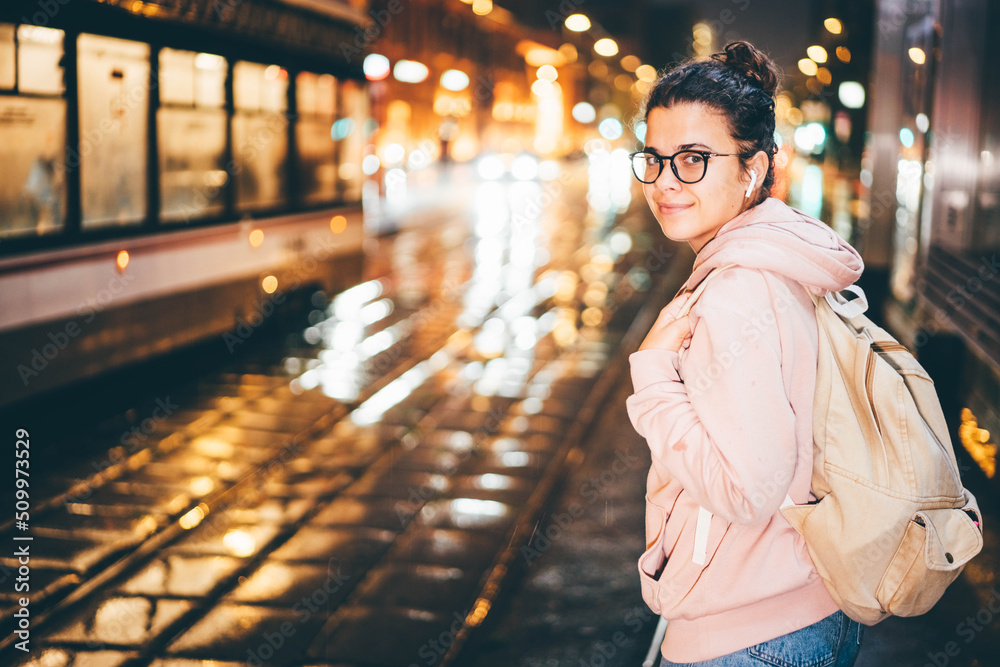 Woman with glasses standing on city transport stop and waiting bus in ...