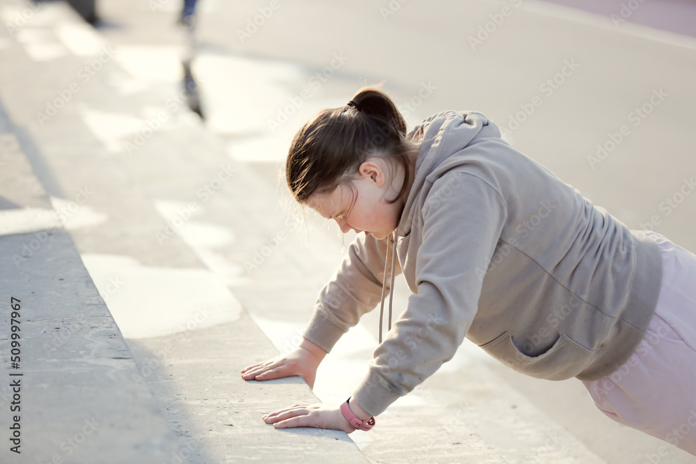 overweight European teenage girl in tracksuit does push-ups on stairs ...