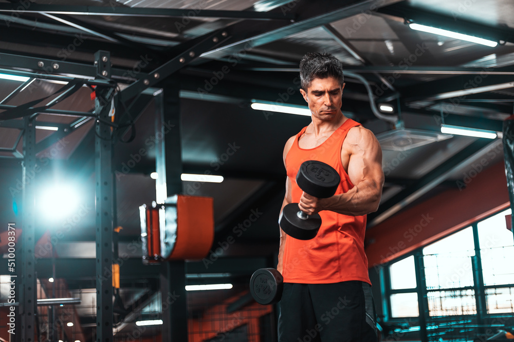 Athlete muscular bodybuilder in the gym training biceps with dumbbell ...