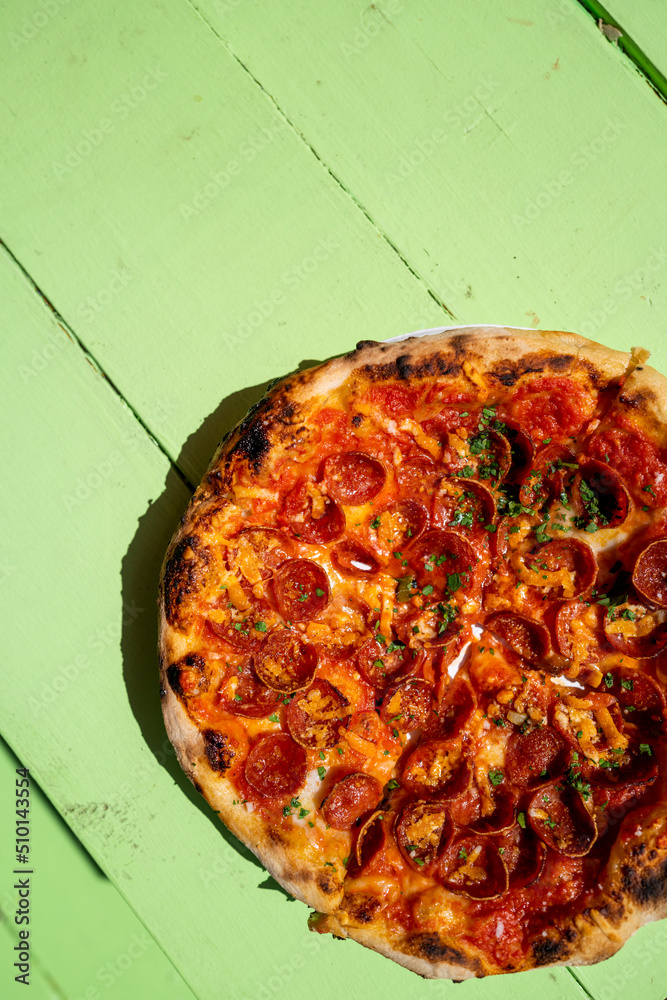 Greasy pepperoni pizza on a green table Stock Photo | Adobe Stock