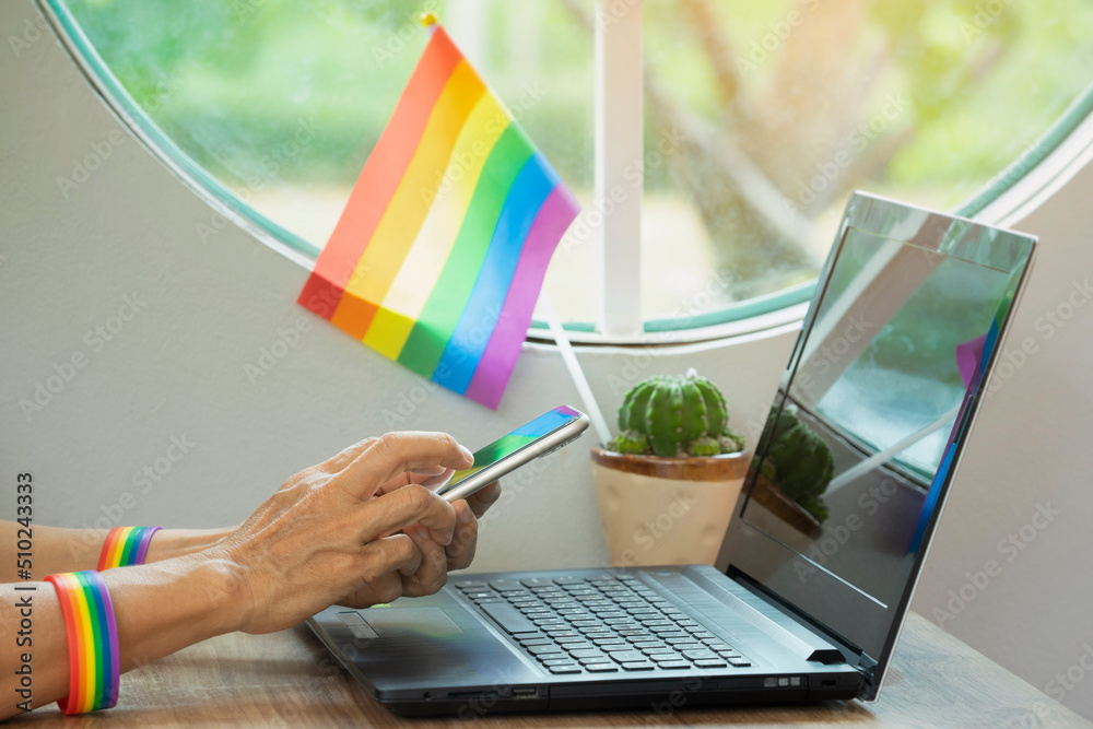 Foto de senior woman hands wear rainbow lgbt wristband is using smartphone,lgbt flag and laptop ...