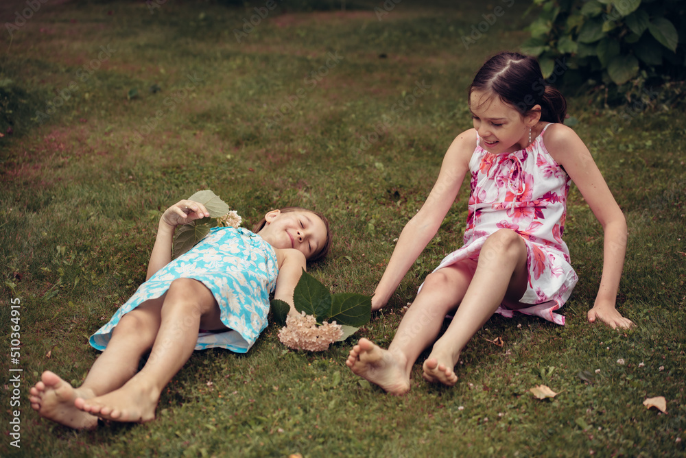 Two little barefoot girls in light summer dresses pose sitting on the ...
