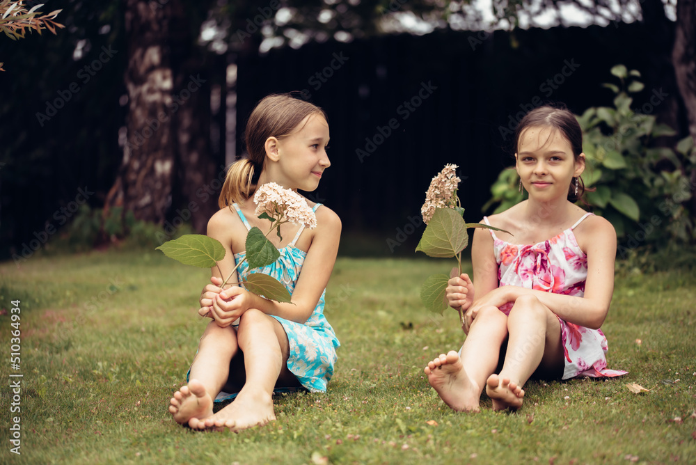 Two little barefoot girls in light summer dresses pose sitting on the ...