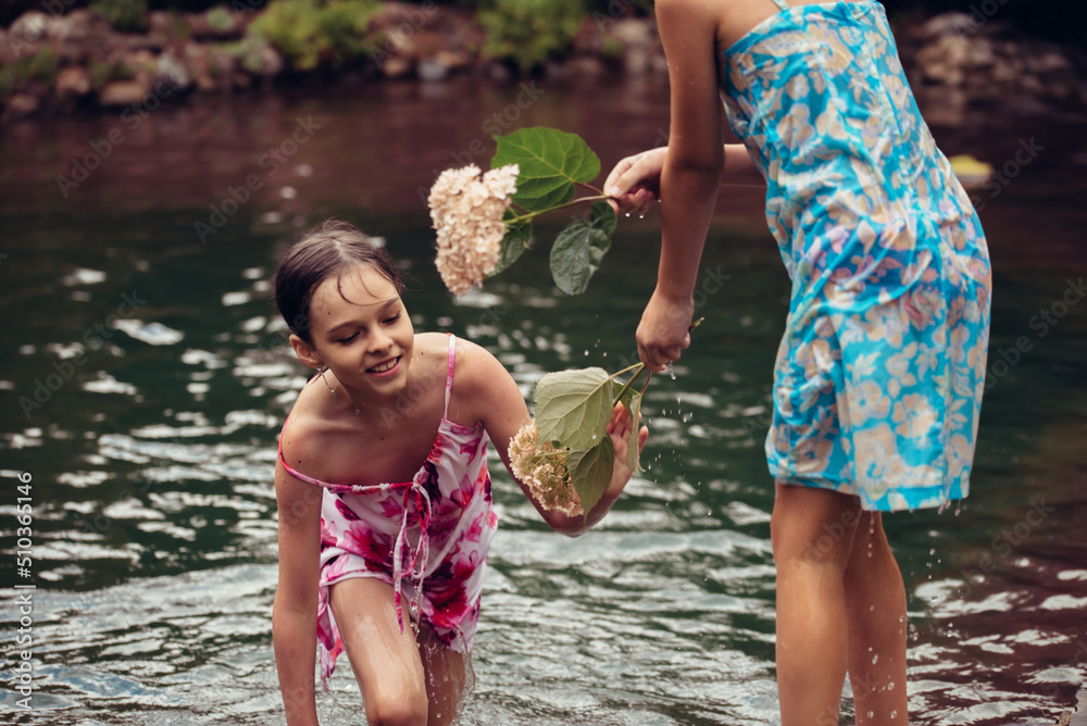 Two little girls in summer dresses swim in a pond outdoors. Children ...