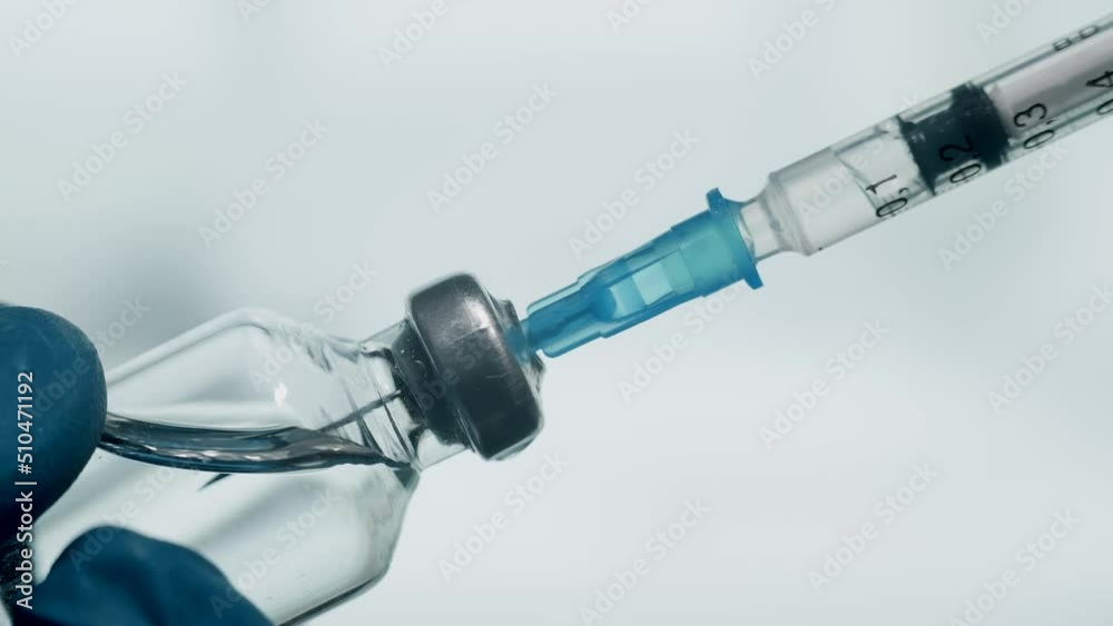 A doctor is drawing up vaccine from phial bottle and filling syringe ...