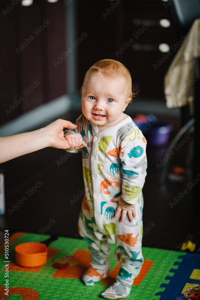 Little nine months baby boy stands with support mother on the rug at ...