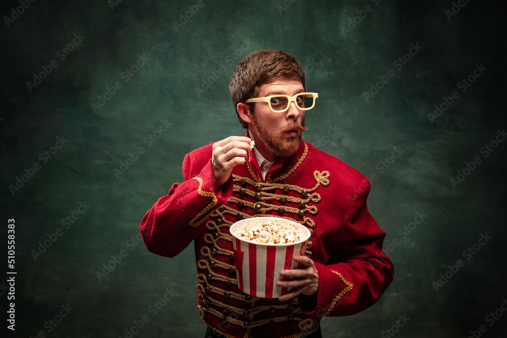Shocked handsome young man in image of medieval hussar eating popcorn ...