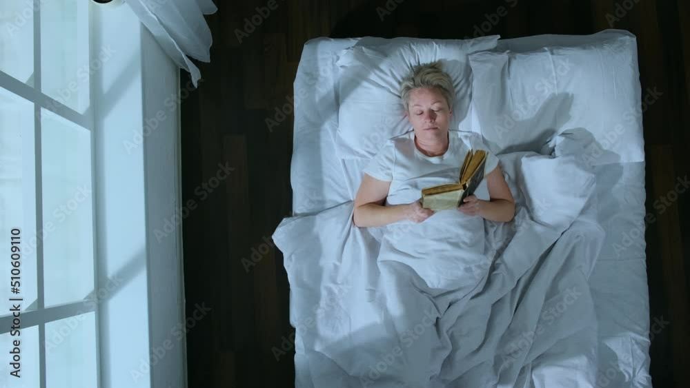 Woman falls asleep while reading book while lying in bed in bedroom ...