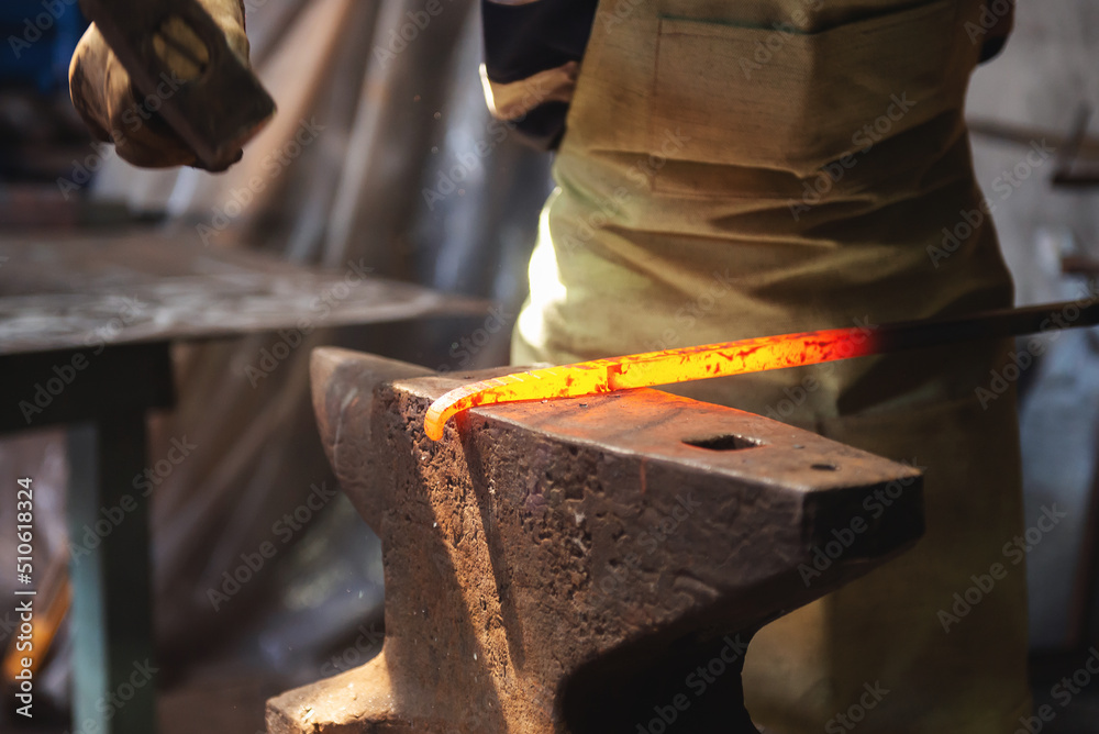 Professional male blacksmith forming red hot metal on an anvil in ...