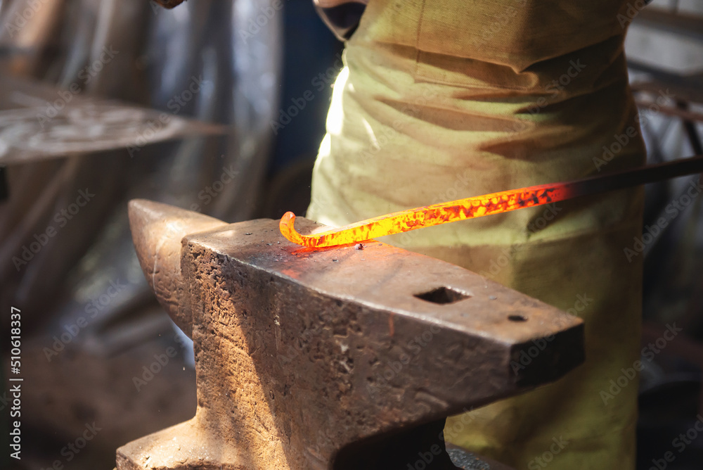 Professional male blacksmith forming red hot metal on an anvil in ...