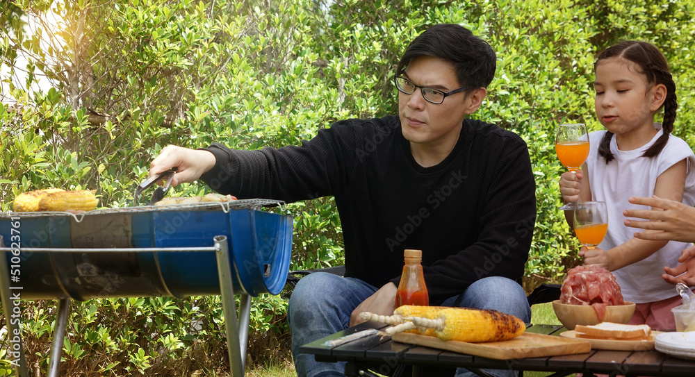 Asian father grills corn and barbecue over a charcoal grill with his ...