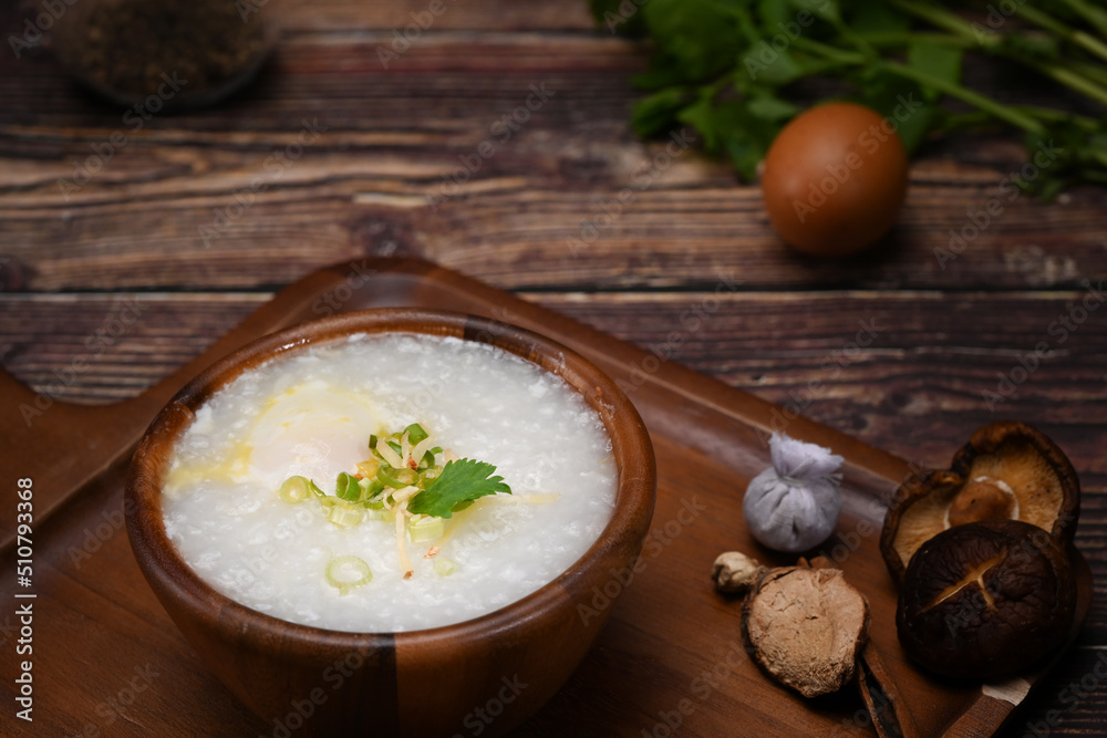 Rice porridge with soft boiled egg, slice ginger and scallion in wooden ...