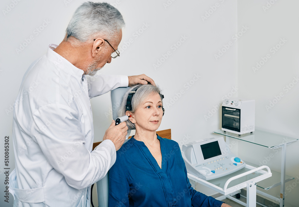 Mature audiologist with tympanometer probe doing procedure tympanometry ...