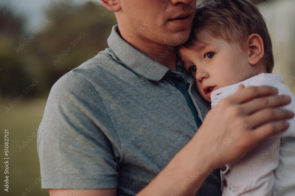 dad soothes a child, his son on a summer day outdoor. little boy crying in his father's arms ...