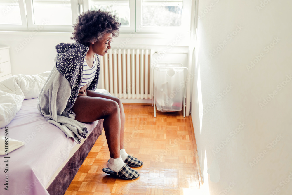Unhealthy young woman with stomachache sitting on the bed at home ...