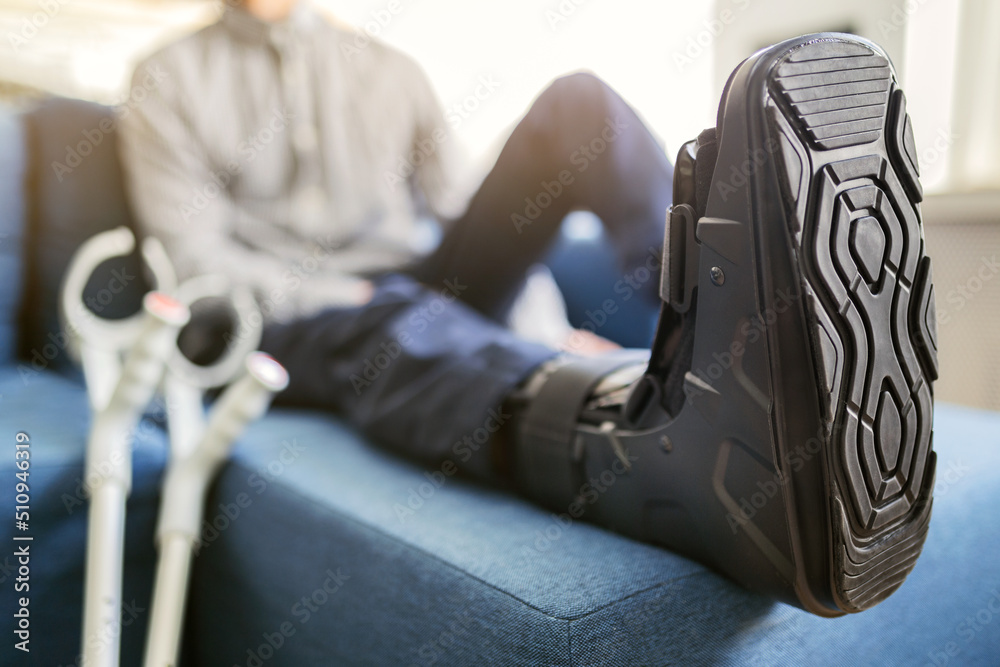 Injuried man with black splint, walker boot, sprained ankle sitting on ...