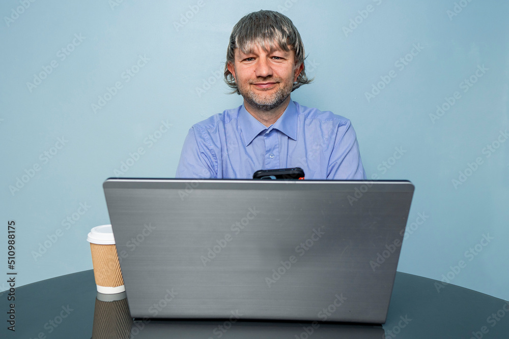 Happy office worker at laptop computer with his phone. Male model ...