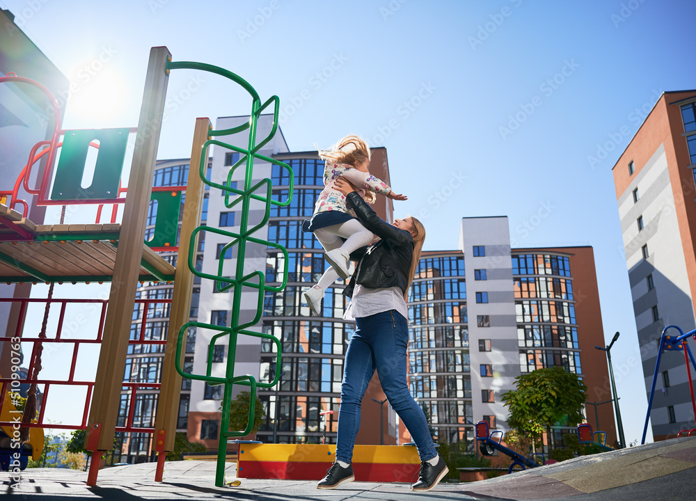 Happy blond mom catching cheerful daughter, jumping from ladder at ...
