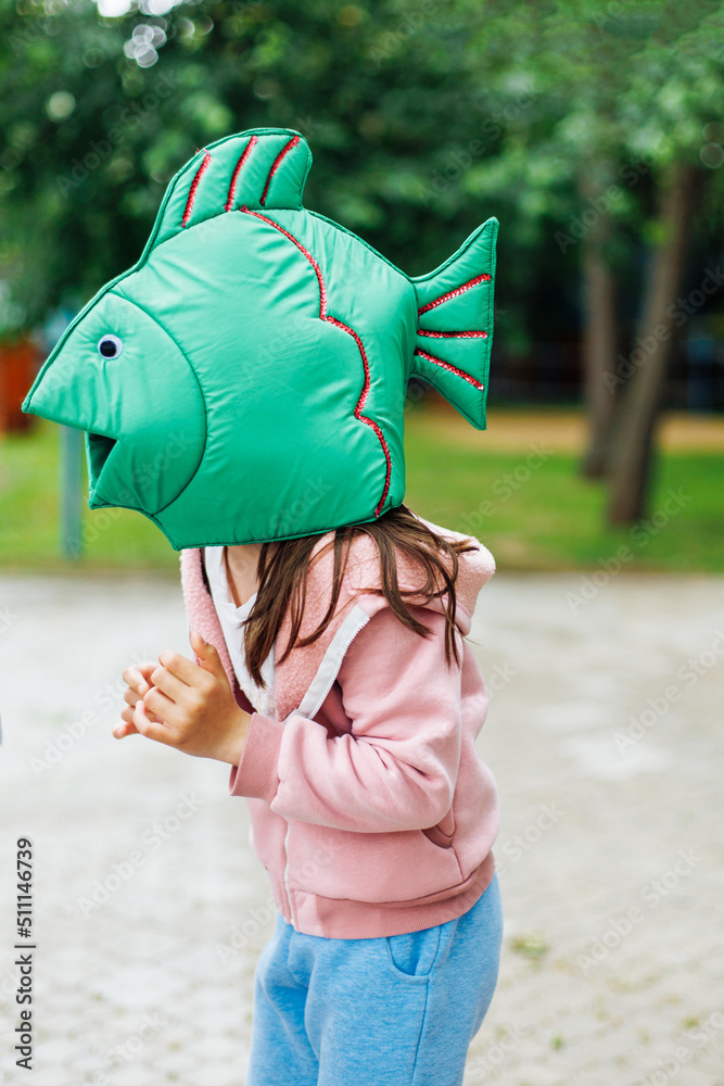 Little girl playing with fish outfit on head in playground in green ...