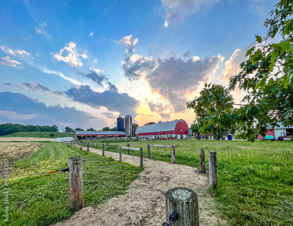A gravel cow lane with a dairy barn and two silos and storm clouds at ...