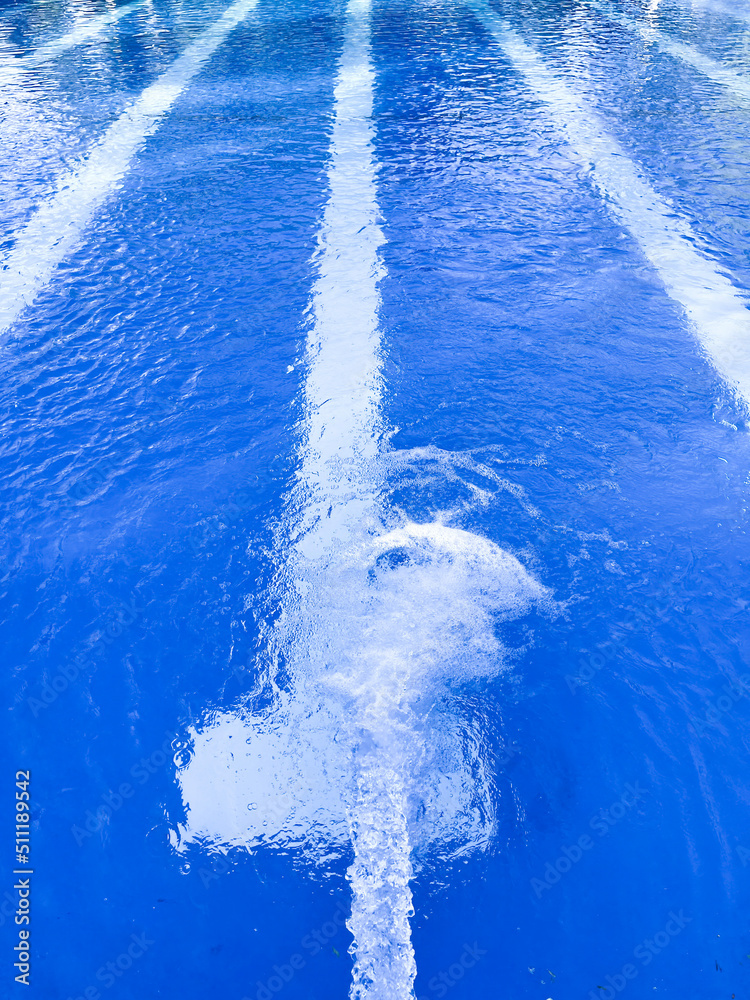 a powerful water jet filling an olympic swimming pool with white lane ...