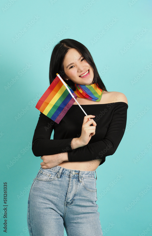 LGBTQ woman holding pride flag standing against a blue green background ...