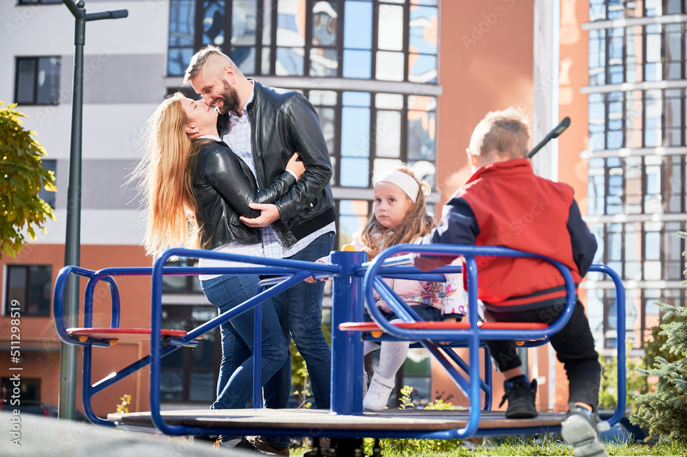 Happy parents hanging out with kids, while children swinging at ...