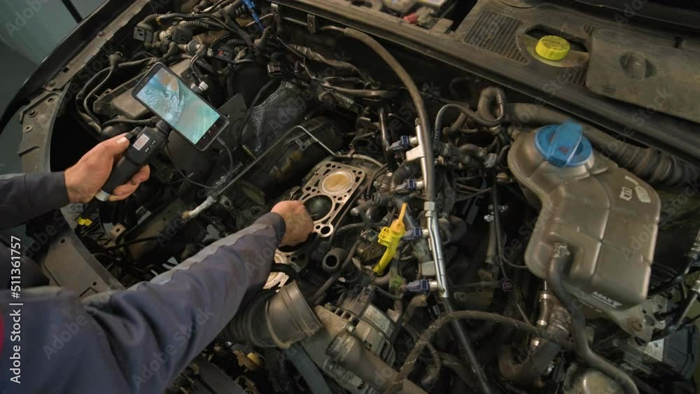 Hands of car mechanic check the vehicle engine with technical endoscope ...