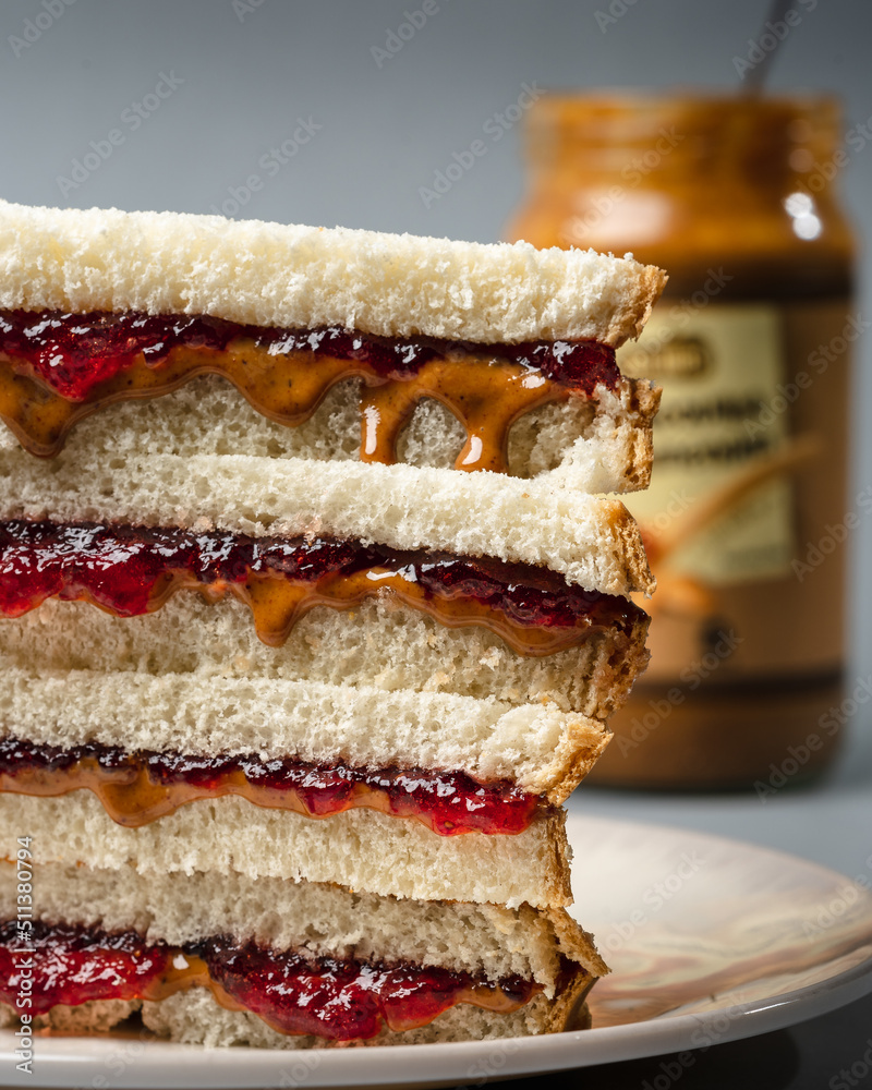 stack of peanut butter and strawberry jelly sandwich and jar of peanut butter out of focus in ...