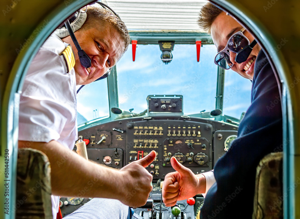 Happy young pilots are smiling and showing thumbs up in the cockpit of ...
