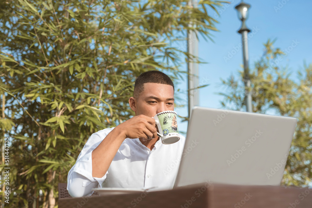 A Filipino male data analyst sips on coffee while working remotely at ...