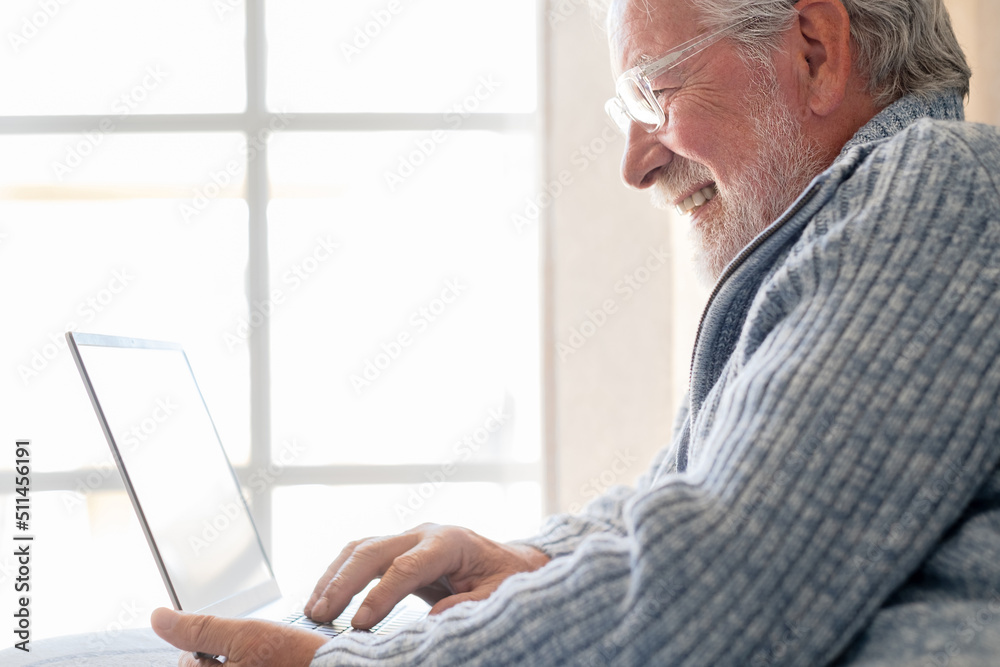 Elderly 70s man seated on sofa browsing on laptop, senior looking at ...