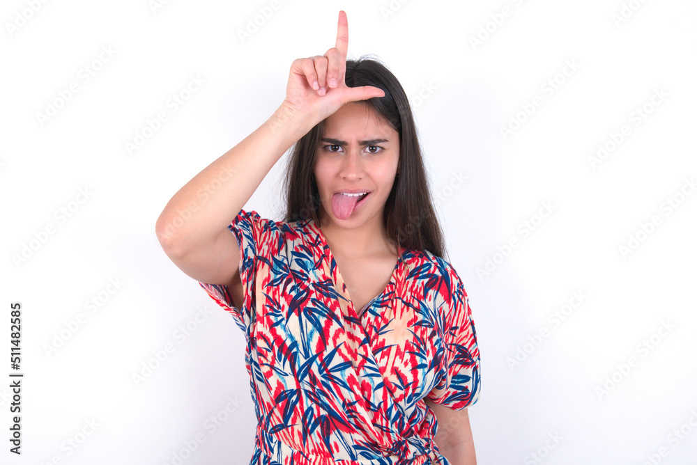 young beautiful brunette woman wearing colourful dress over white wall ...