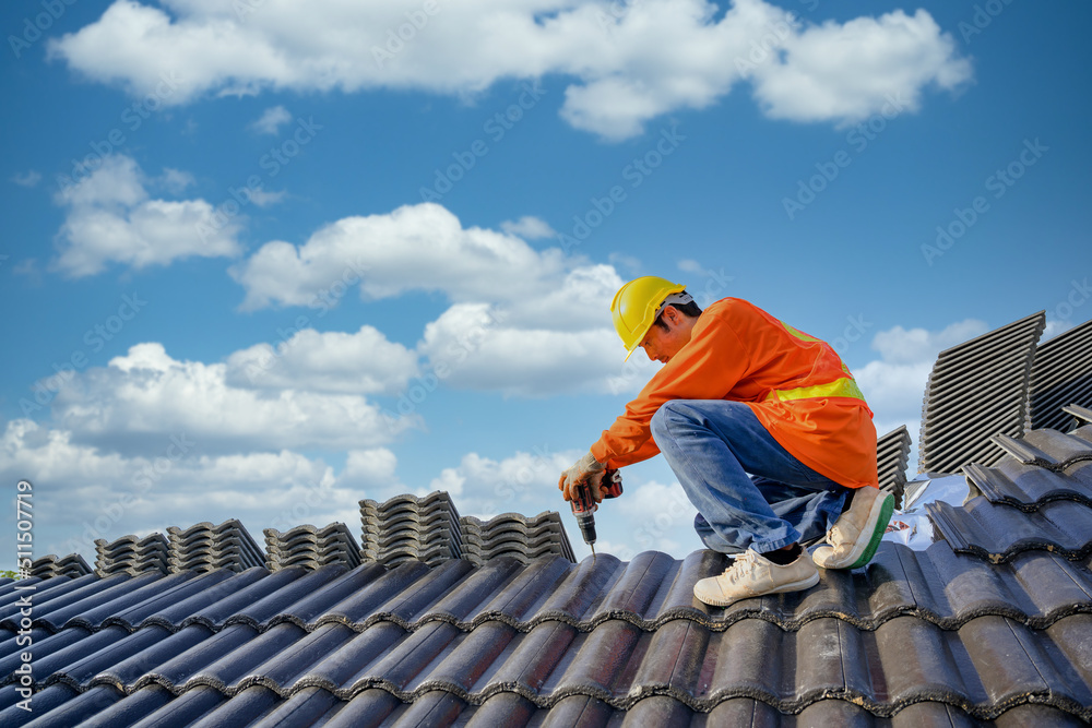 A male roofing installer is working on the roof of a house ...