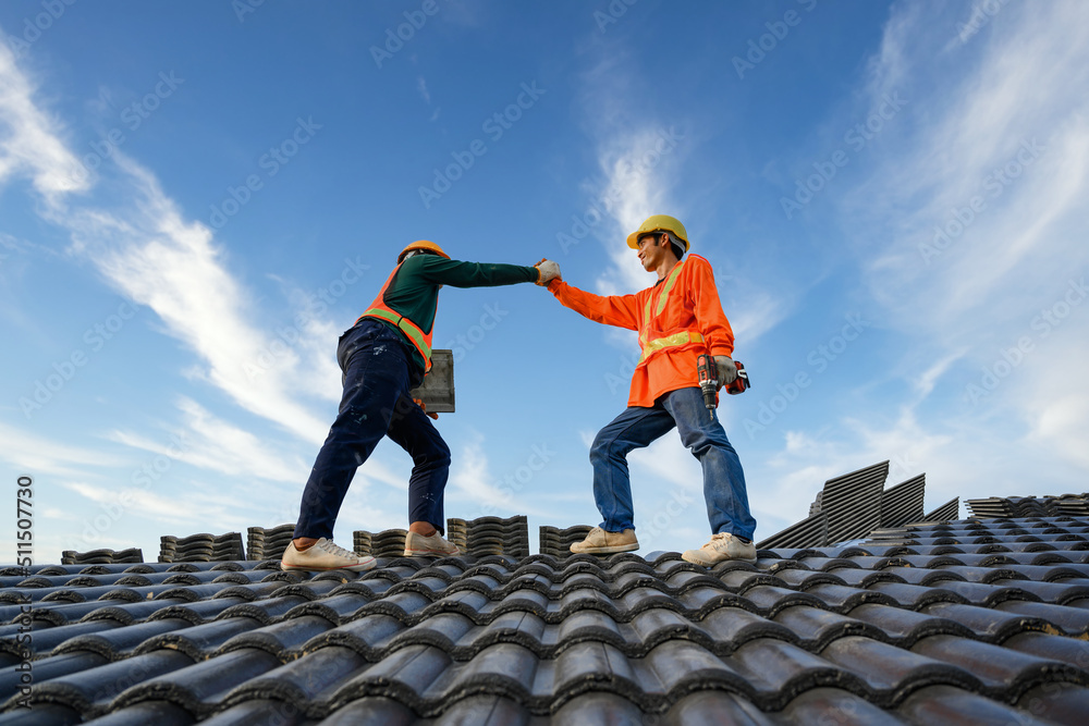 male roof installer construction workers on the roof working as a team ...