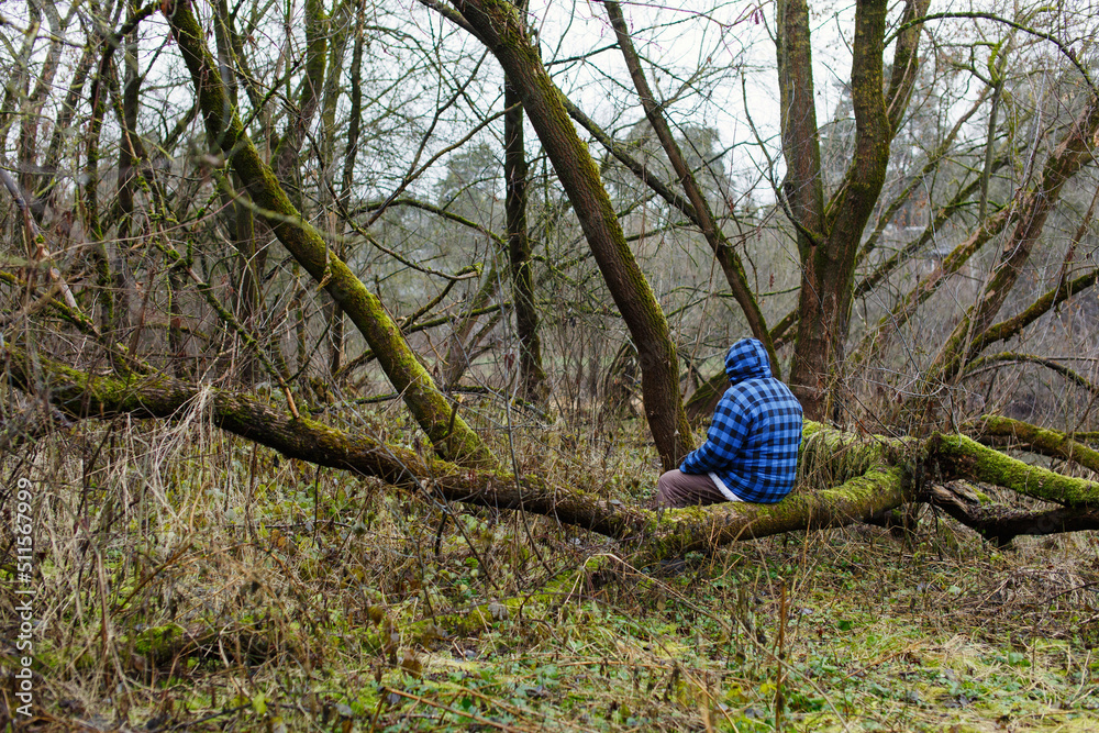 lonely old fat man sitting resting on a tree with moss in the woods ...