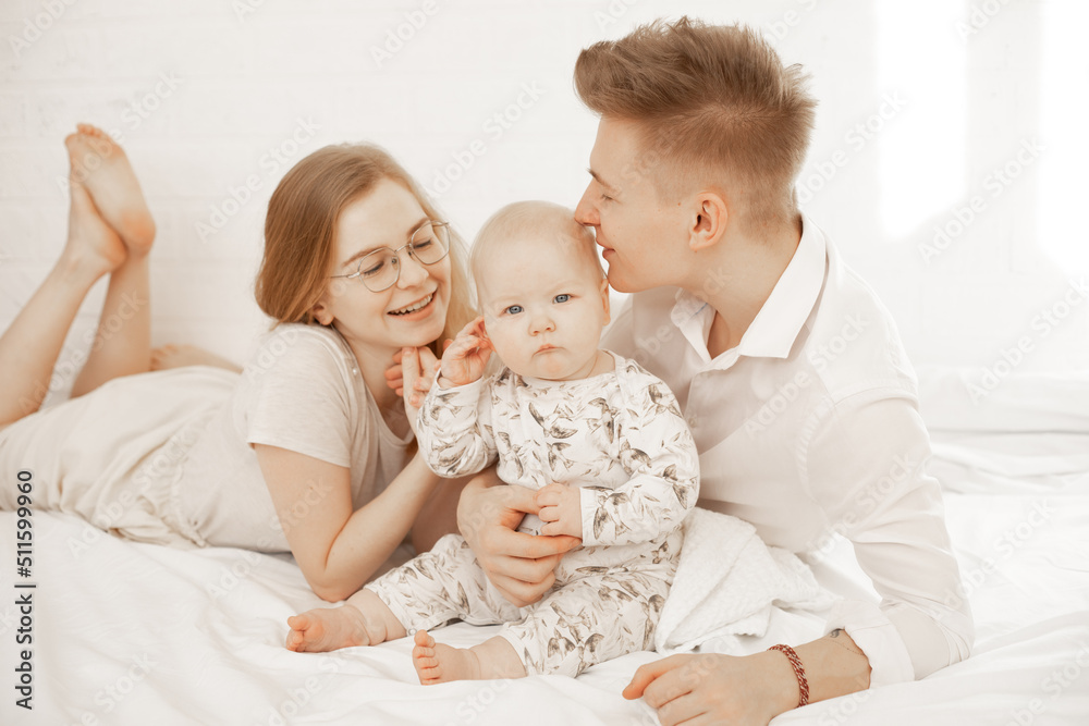 Young mother and father lay with little baby on bed, embrace and enjoy ...