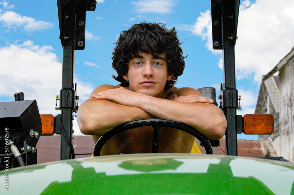 Young athletic young farm boy is resting on his tractor as he gets ...