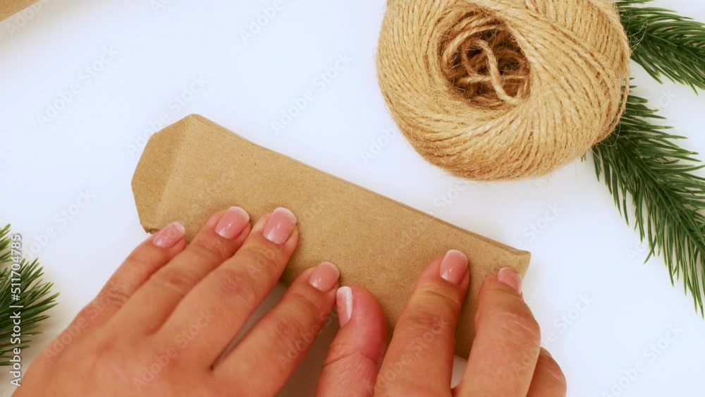 Unrecognizable woman wrapping gift box with brown kraft paper on white ...